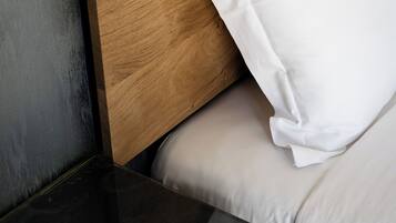 Uma cama com cabeceira de madeira, roupa de cama branca e mesa de cabeceira escura e espelhada.