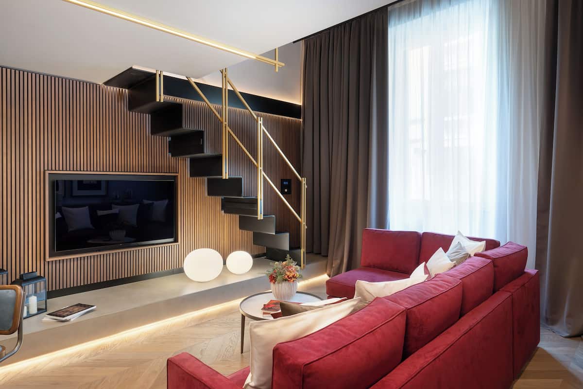 Uma sala de estar moderna com um sofá vermelho, uma TV de tela plana, uma escada e uma janela grande com cortinas.