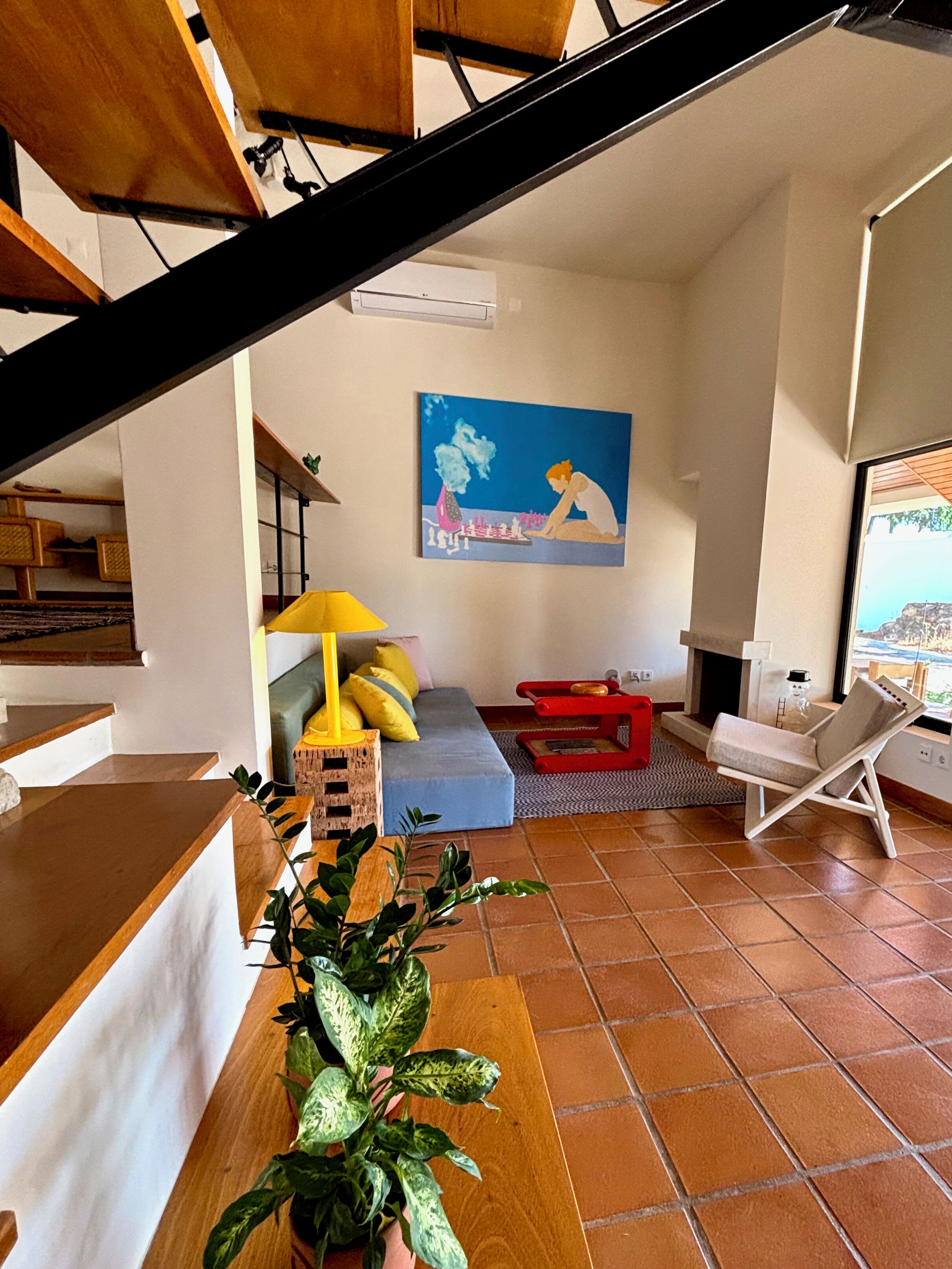 Sala de estar moderna com escada, um quadro na parede, sofá e uma cadeira vermelha, além de uma planta.
