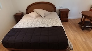 Quarto com cama, duas mesas de cabeceira, cabeceira de madeira, janela e uma pequena mesa redonda.