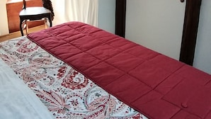 Quarto com cama, cadeira, porta com ganchos e janela com cortinas.