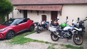 Um SUV vermelho estacionado em frente a um edifício com telhado de azulejos e uma motocicleta à frente.