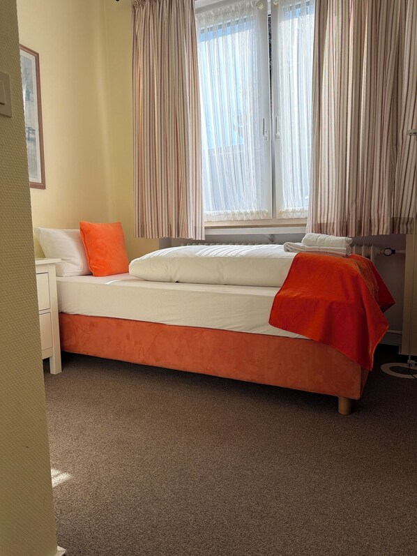Um quarto com cama, mesa de cabeceira, cômoda e janela com cortinas.