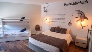 Quarto com cama de solteiro, uma cama individual, parede com mural de David Machado e uma cadeira pequena.