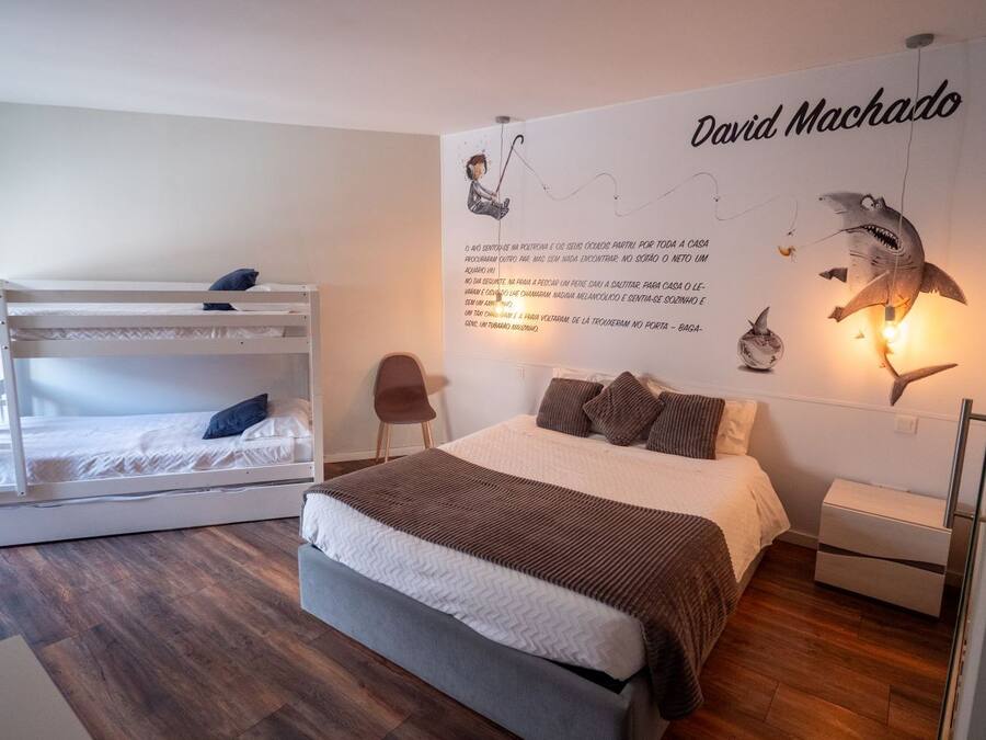 Quarto com cama de solteiro, uma cama individual, parede com mural de David Machado e uma cadeira pequena.