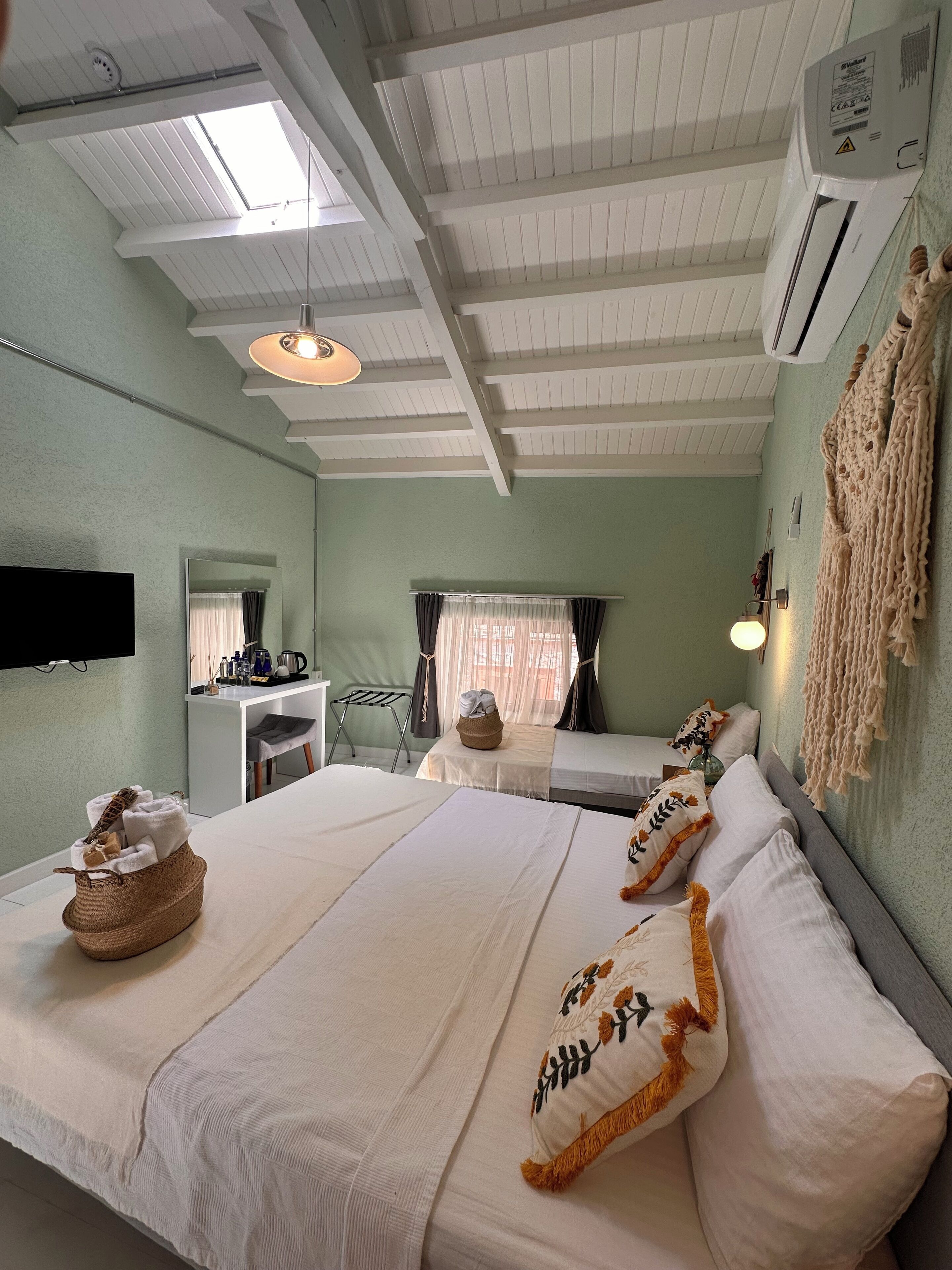 Quarto de hotel com uma cama grande, uma escrivaninha pequena, um espelho e uma janela com cortinas.