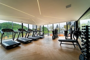 Academia com esteiras, aparelhos de musculação e vista para o verde através de amplas janelas.
