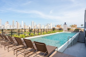 Piscina no terraço com cadeiras de descanso, vista para o horizonte urbano e escada que leva a um andar superior.