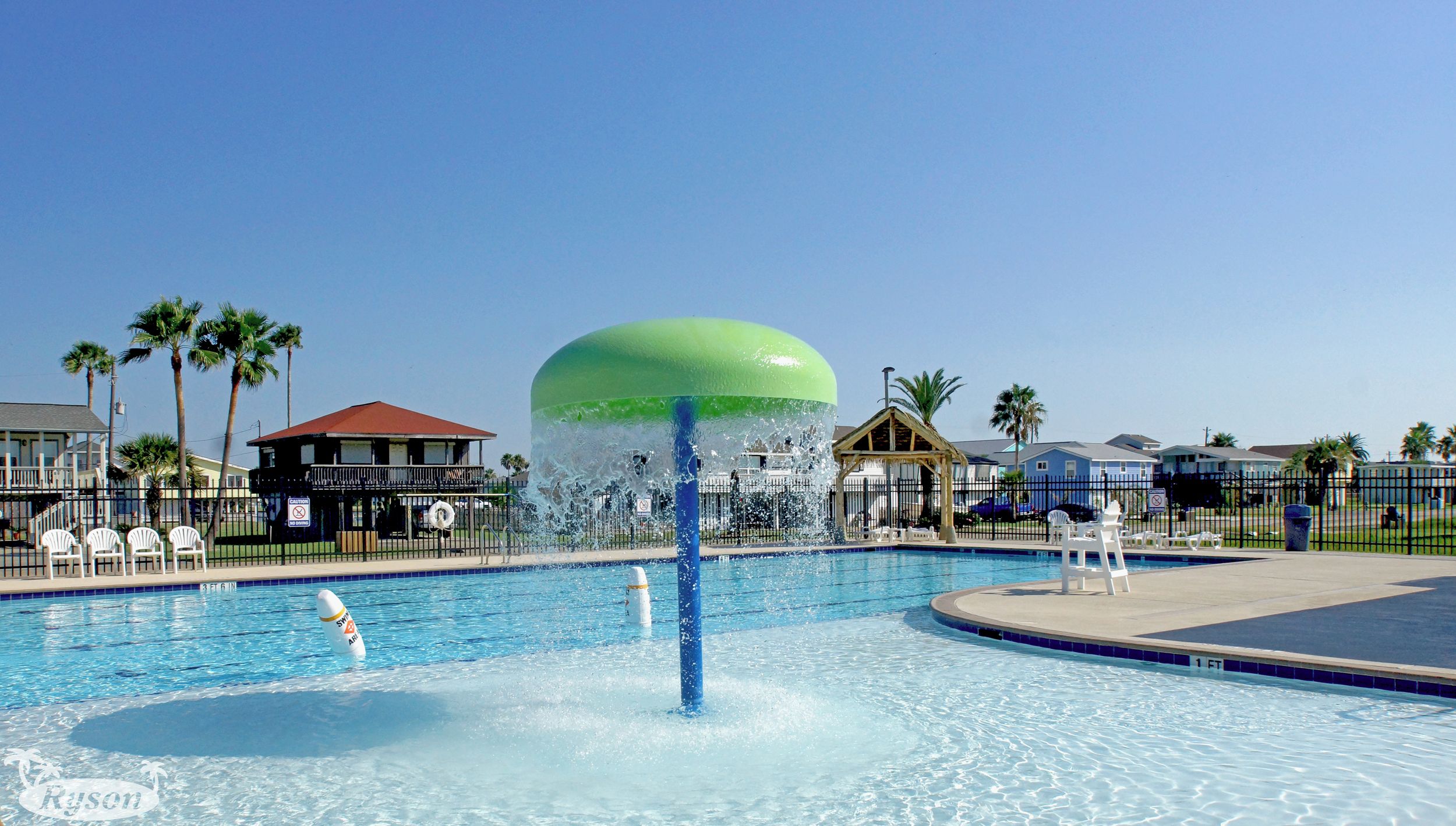 Uma piscina com fonte, palmeiras e casas ao fundo.