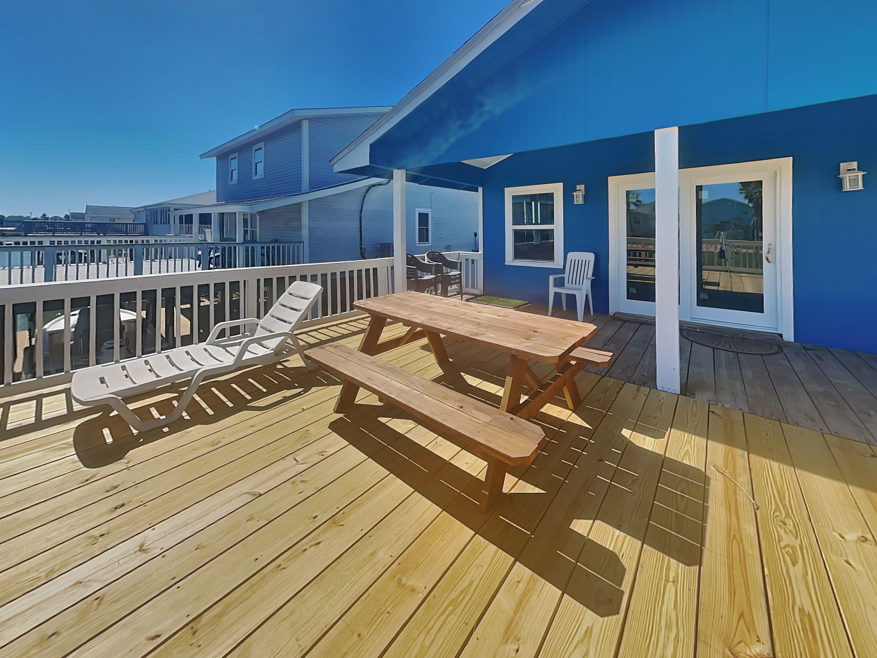 Um deck de madeira com mesa de piquenique e cadeiras de lounge, com vista para um corpo d'água.