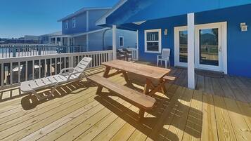 Um deck de madeira com mesa de piquenique e cadeiras de lounge, com vista para um corpo d'água.