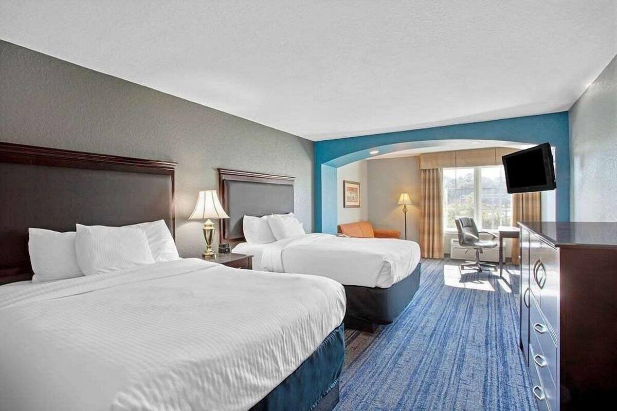 Quarto de hotel com duas camas, uma escrivaninha, uma cadeira, uma televisão e vista para o exterior.