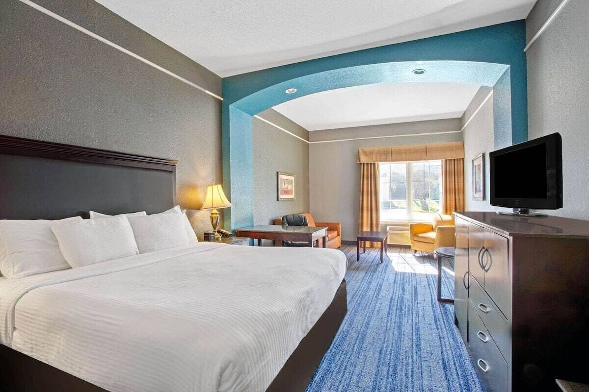 Quarto de hotel com cama grande, escrivaninha, cadeira, televisão e vista para o exterior.