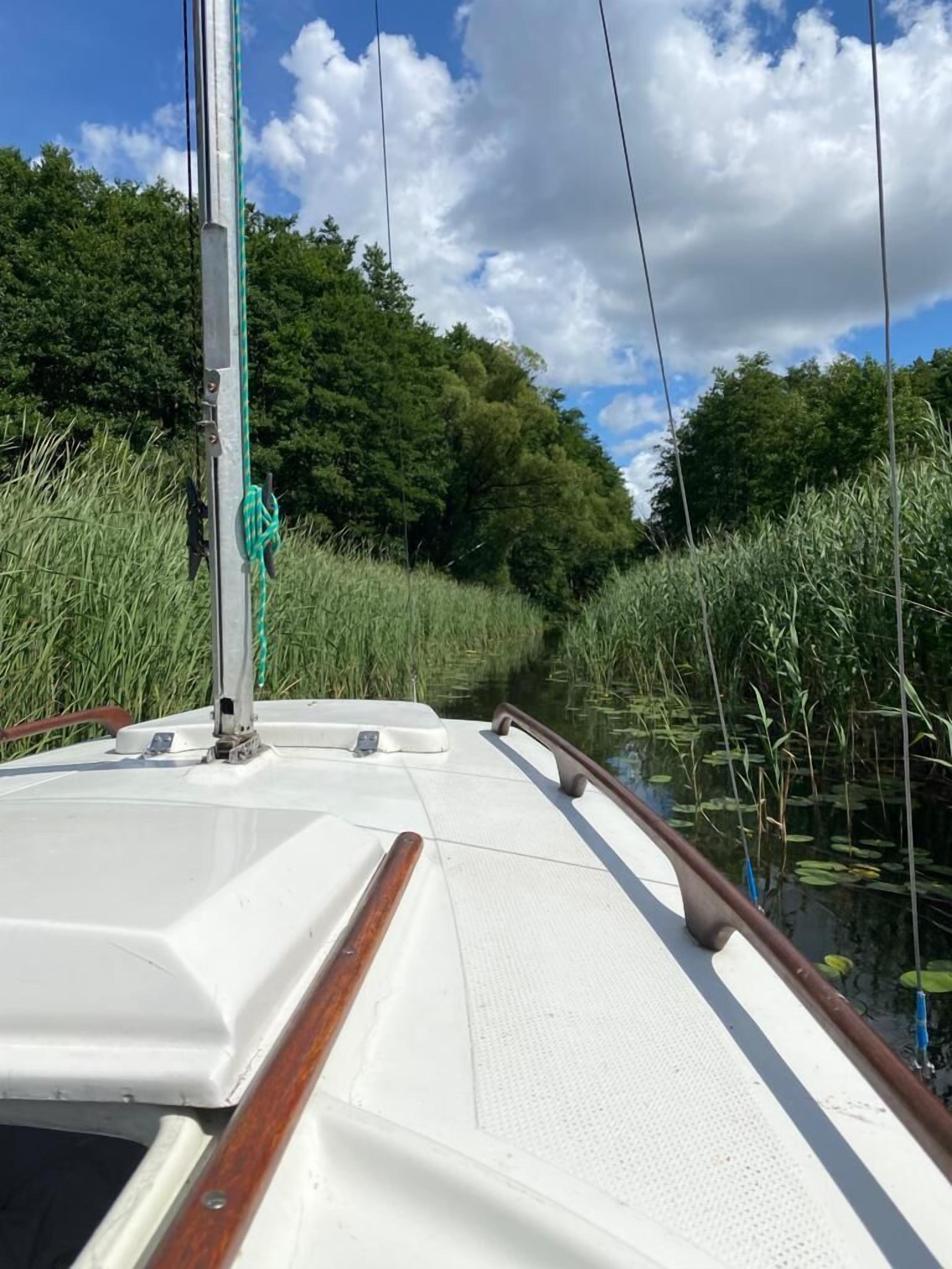 Convés de barco com superfície branca, guarda-corpo de metal e corda verde amarrada ao guarda-corpo.