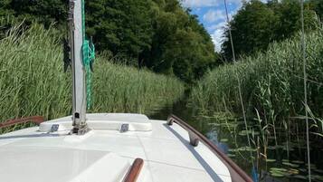 Convés de barco com superfície branca, guarda-corpo de metal e corda verde amarrada ao guarda-corpo.