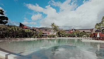 Um resort com uma piscina grande, vários edifícios com telhados vermelhos e vegetação exuberante.