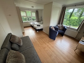 Quarto com sofá, duas camas, uma poltrona e janelas amplas com vista para o verde.