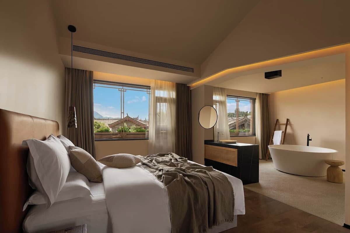 Quarto de hotel moderno com uma cama grande, banheiro com banheira e vista para arquitetura tradicional.