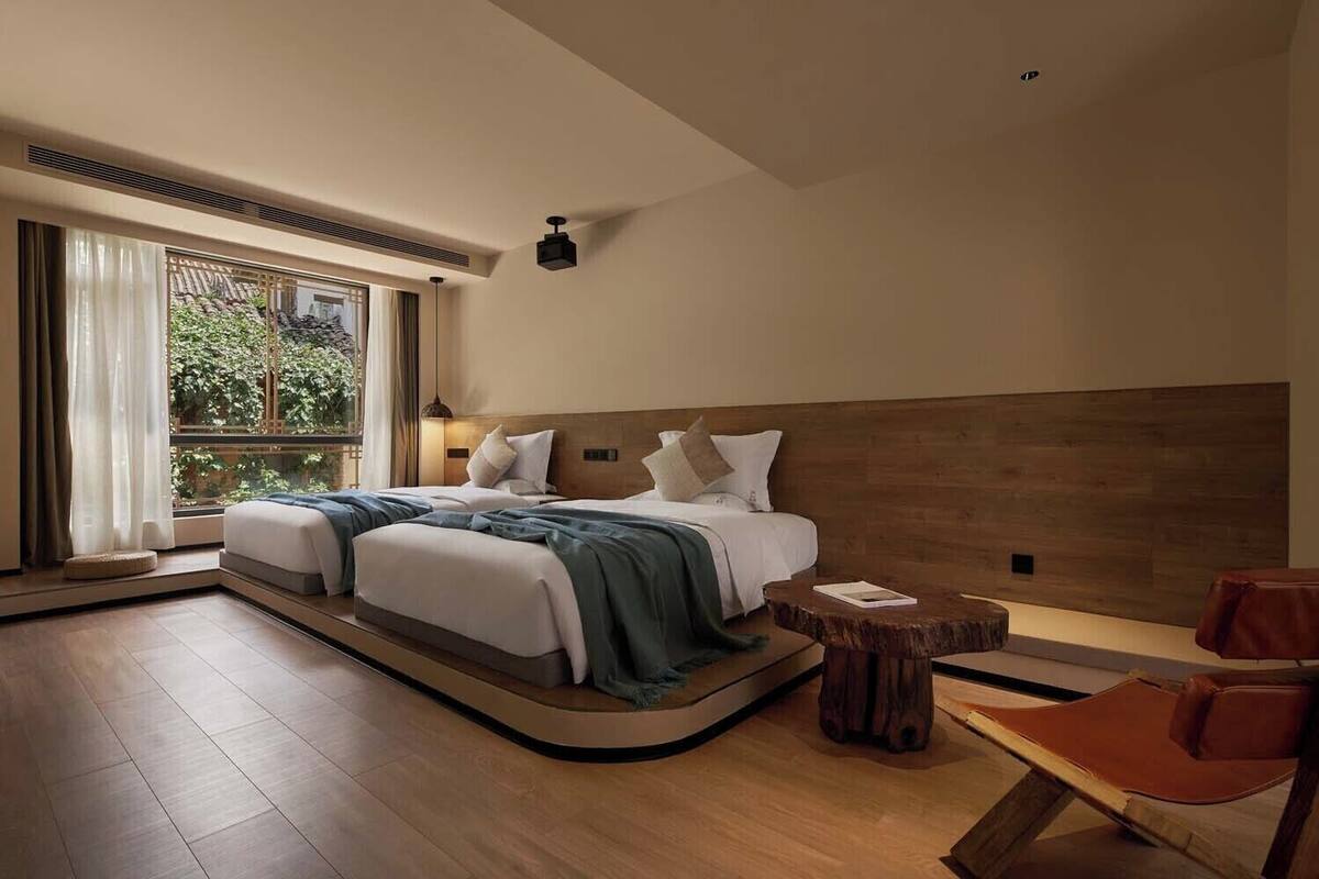 Quarto moderno com uma cama grande, cabeceira de madeira, mesa de cabeceira pequena em madeira e vista para o verde lá fora.