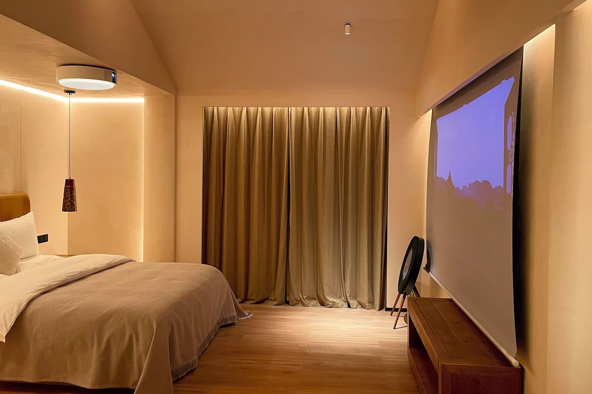 Quarto de hotel moderno com uma cama grande, televisão de tela plana e tela de projeção.