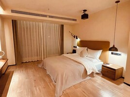 Quarto de hotel com uma cama grande, mesa de cabeceira, projetor no teto e janela com cortinas.