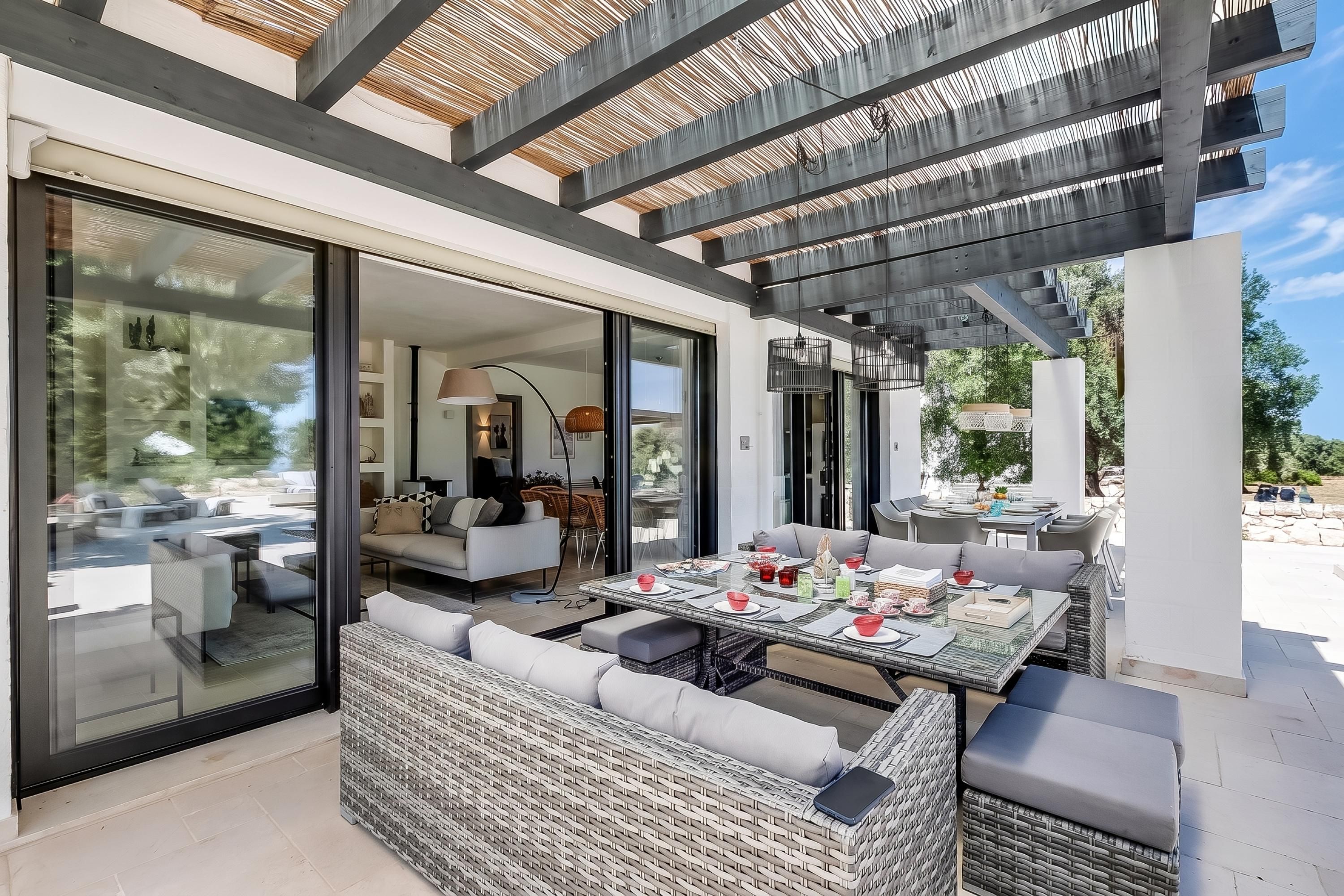 Uma área de refeições moderna ao ar livre, com estrutura de vidro, móveis de vime e uma pérgola.