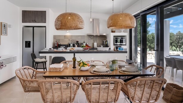 Uma cozinha moderna com área de jantar, com luminárias pendentes de vime, uma janela grande e vista para o exterior.