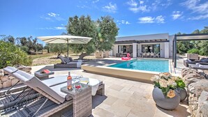 Uma área moderna de piscina ao ar livre com espreguiçadeiras, espaço para refeições e um pérgola.