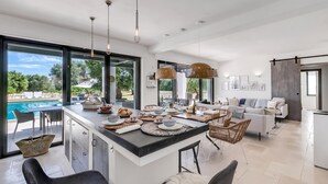 Uma cozinha moderna com uma ilha grande, área de jantar e vista para uma piscina.