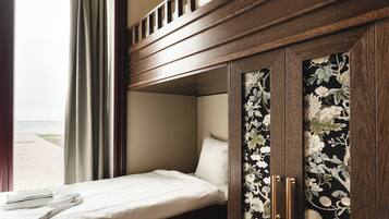 Uma cama de solteiro com cabeceira de madeira, uma janela com cortinas e um guarda-roupa com papel de parede floral.