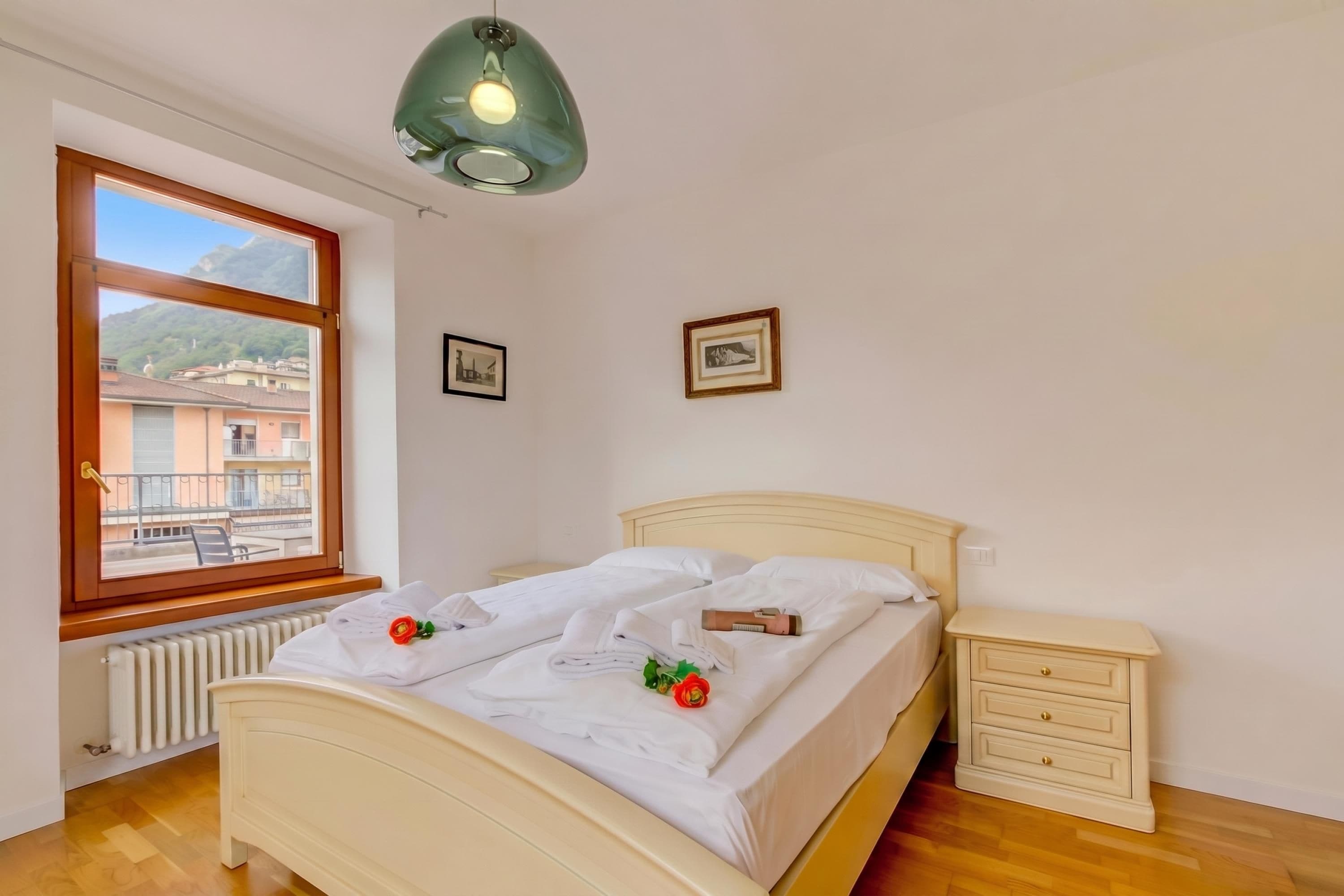 Quarto de hotel com uma cama, uma mesa de cabeceira, um radiador, uma janela com vista para edifícios e um candeeiro suspenso.