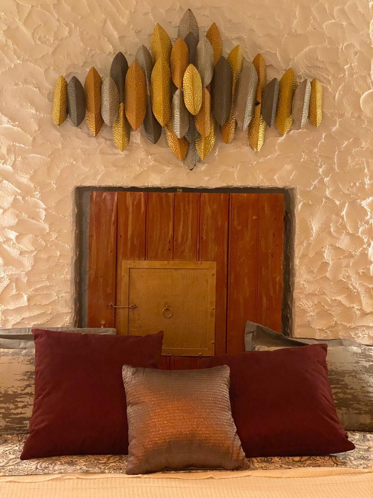 Um quarto com parede texturizada, porta de madeira e duas almofadas vermelhas na cama.