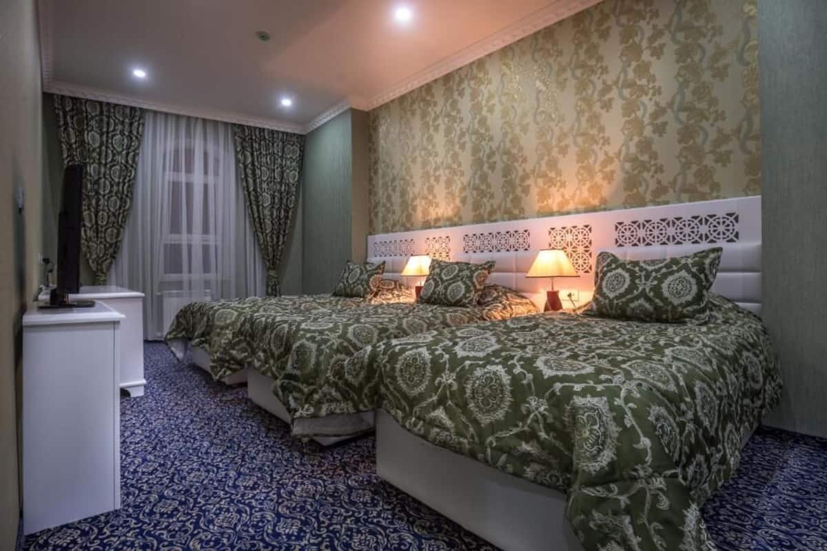 Quarto de hotel com duas camas, uma escrivaninha e um tapete estampado.