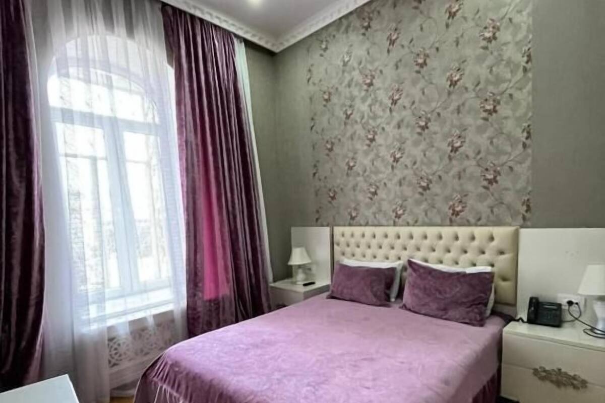 Quarto com cama, mesas de cabeceira, janela com cortinas e papel de parede floral.