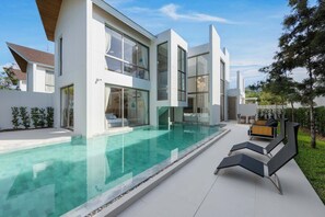 Uma casa moderna de dois andares, com piscina, área de estar externa e um jardim bem cuidado.