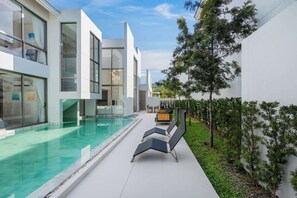 Uma área de piscina moderna ao ar livre, com piscina envidraçada, espreguiçadeiras e um terraço com vista para os edifícios circundantes.