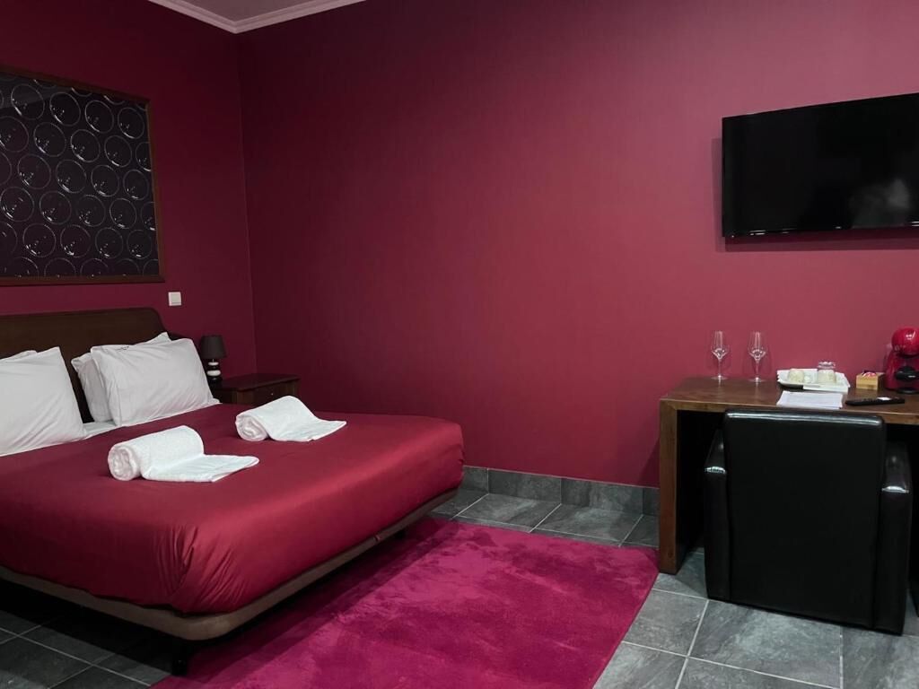 Quarto de hotel com uma cama grande, uma escrivaninha com cadeira, uma TV de tela plana e um tapete vermelho.