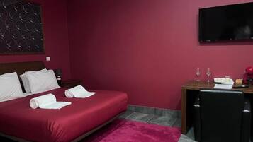 Quarto de hotel com uma cama grande, uma escrivaninha com cadeira, uma TV de tela plana e um tapete vermelho.