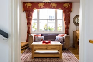 Um quarto aconchegante com sofá, mesa de centro de madeira e janela com cortinas.