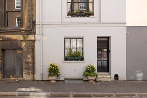 Um edifício com fachada branca, porta preta e uma janela com floreira.