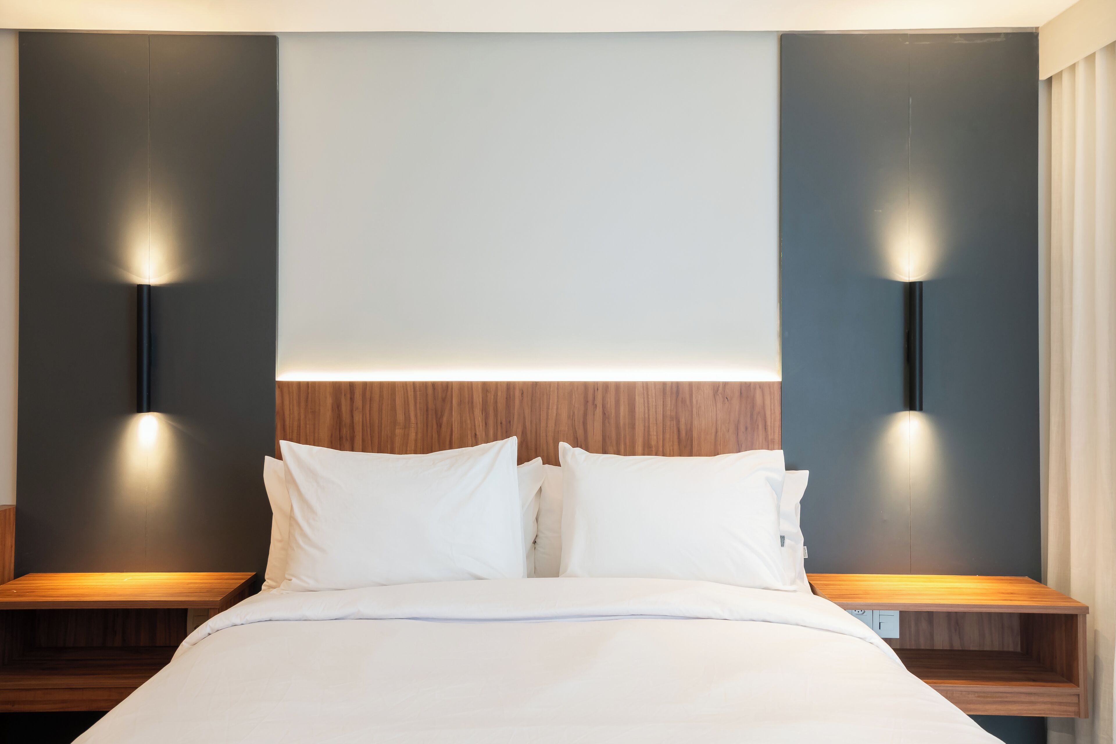 Quarto de hotel com uma cama grande, duas mesas de cabeceira e iluminação embutida na parede.