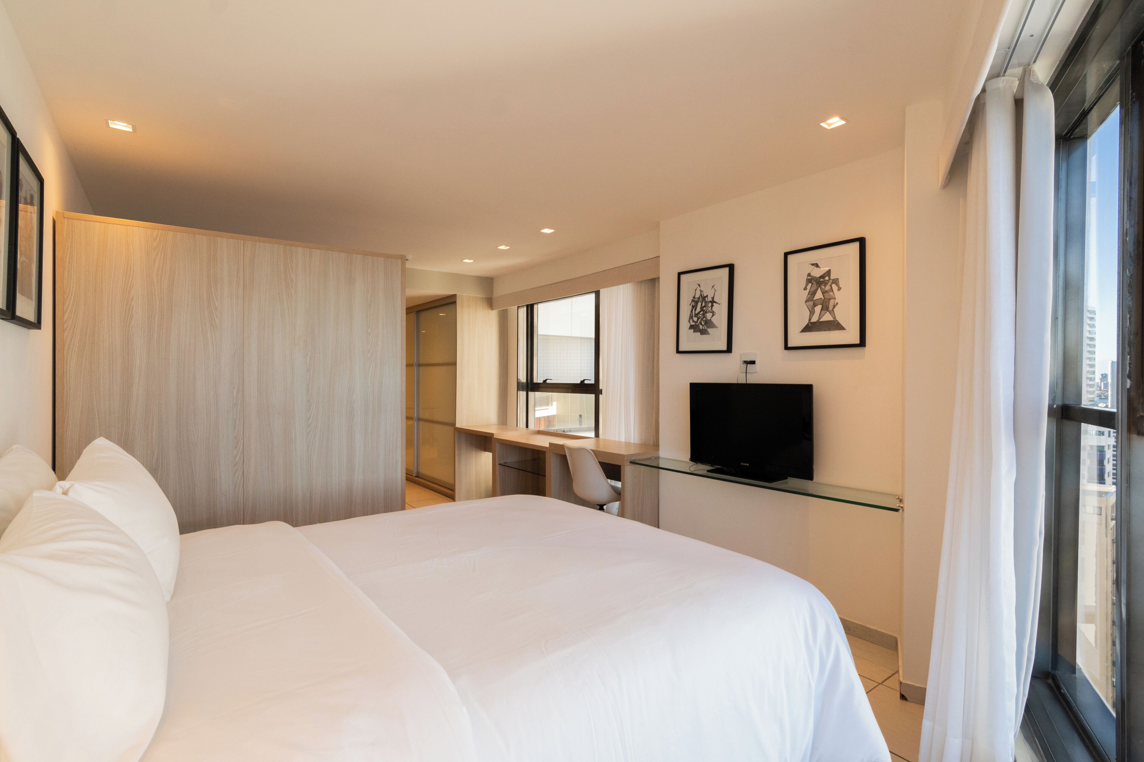 Quarto de hotel com cama, escrivaninha, televisão e obras de arte nas paredes.
