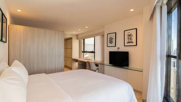 Quarto de hotel com cama, escrivaninha, televisão e obras de arte nas paredes.