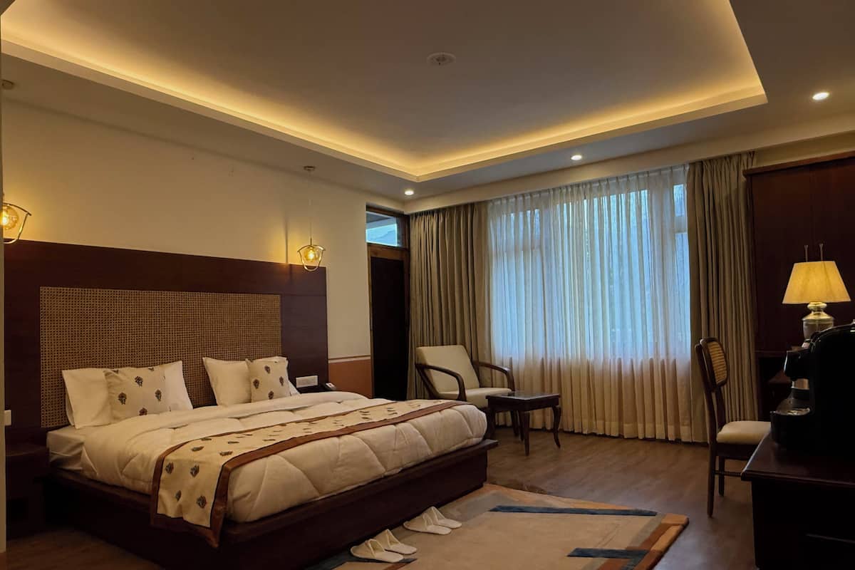 Quarto de hotel com uma cama grande, uma escrivaninha, uma cadeira e uma janela com cortinas.