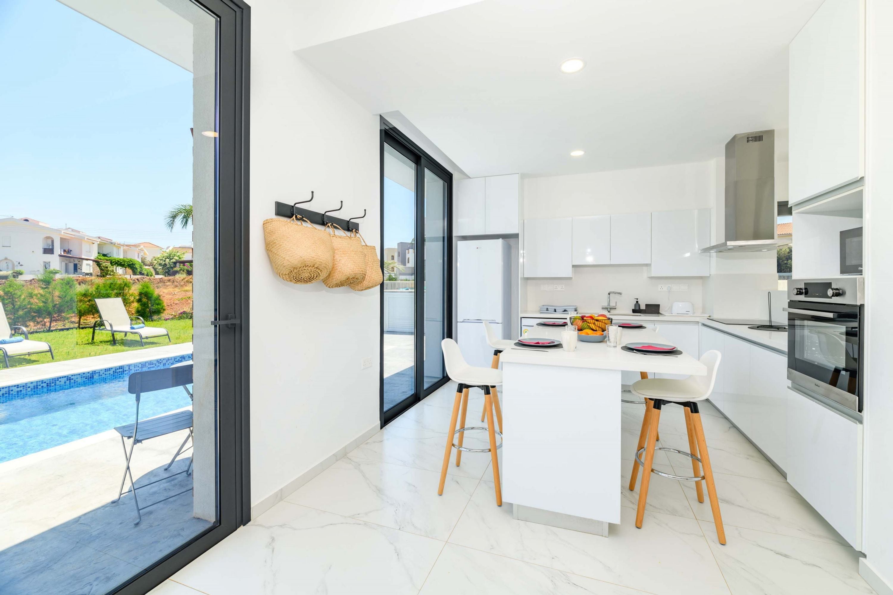 Uma cozinha moderna com armários brancos, uma ilha central e vista para uma piscina.