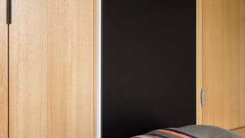Quarto com guarda-roupa de madeira, porta preta, cama para animais de estimação cinza com listras e um comedouro branco em suporte.