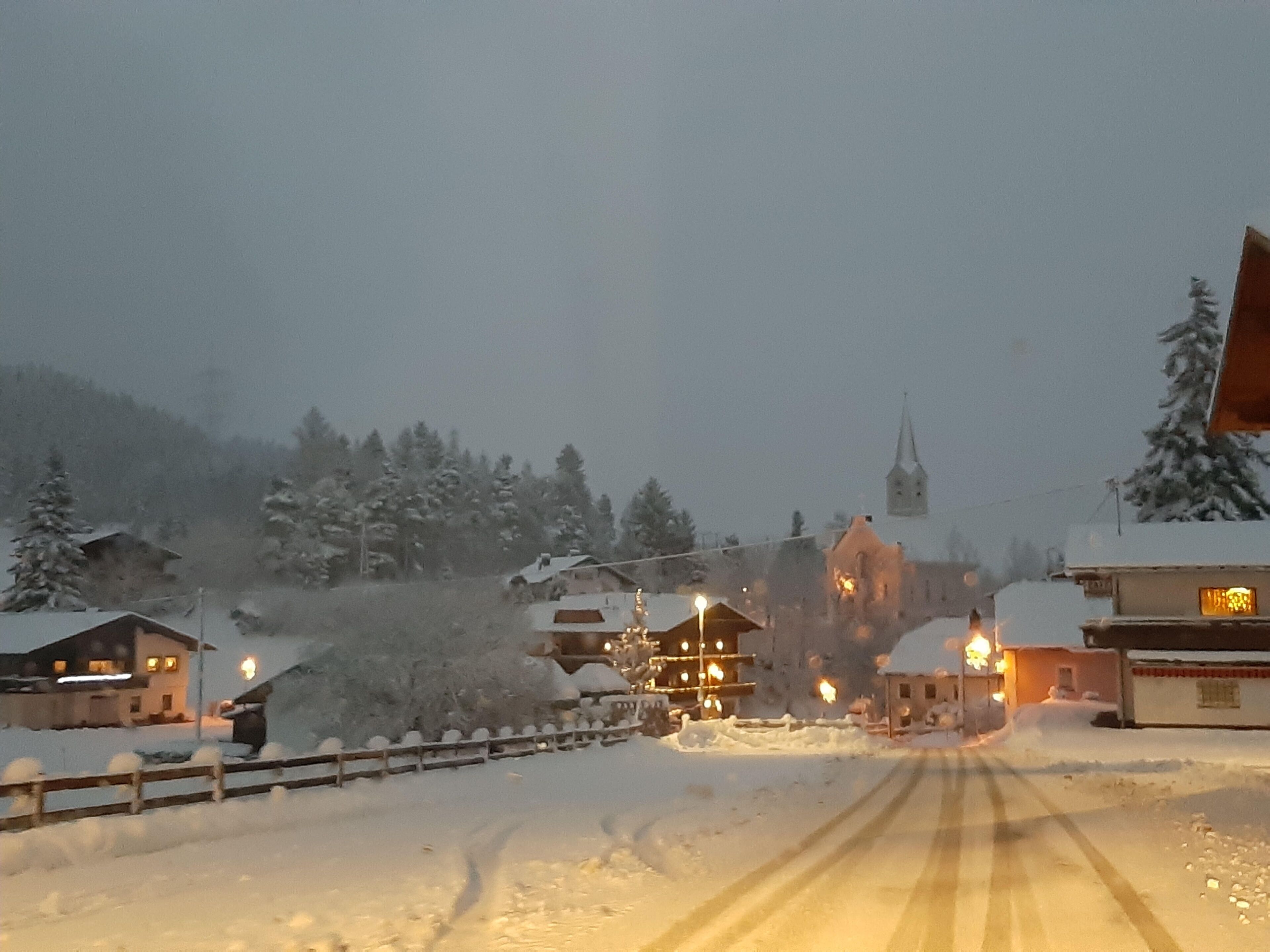 Uma aldeia coberta de neve com edifícios, uma igreja e uma estrada.