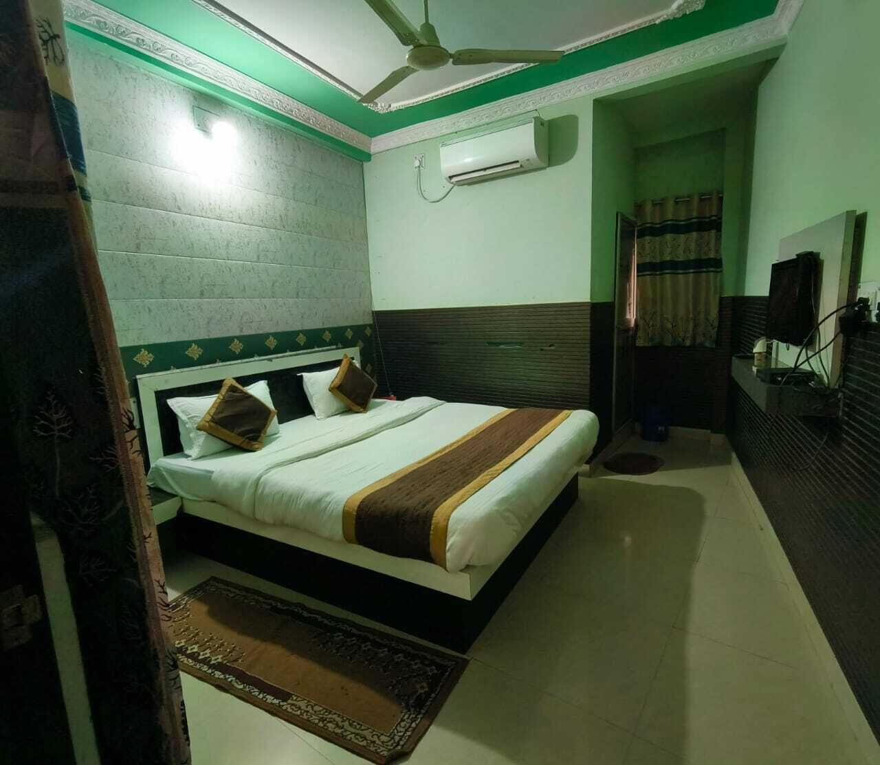 Quarto de hotel com cama, ventilador de teto, ar condicionado, banheiro com chuveiro e uma pequena mesa.