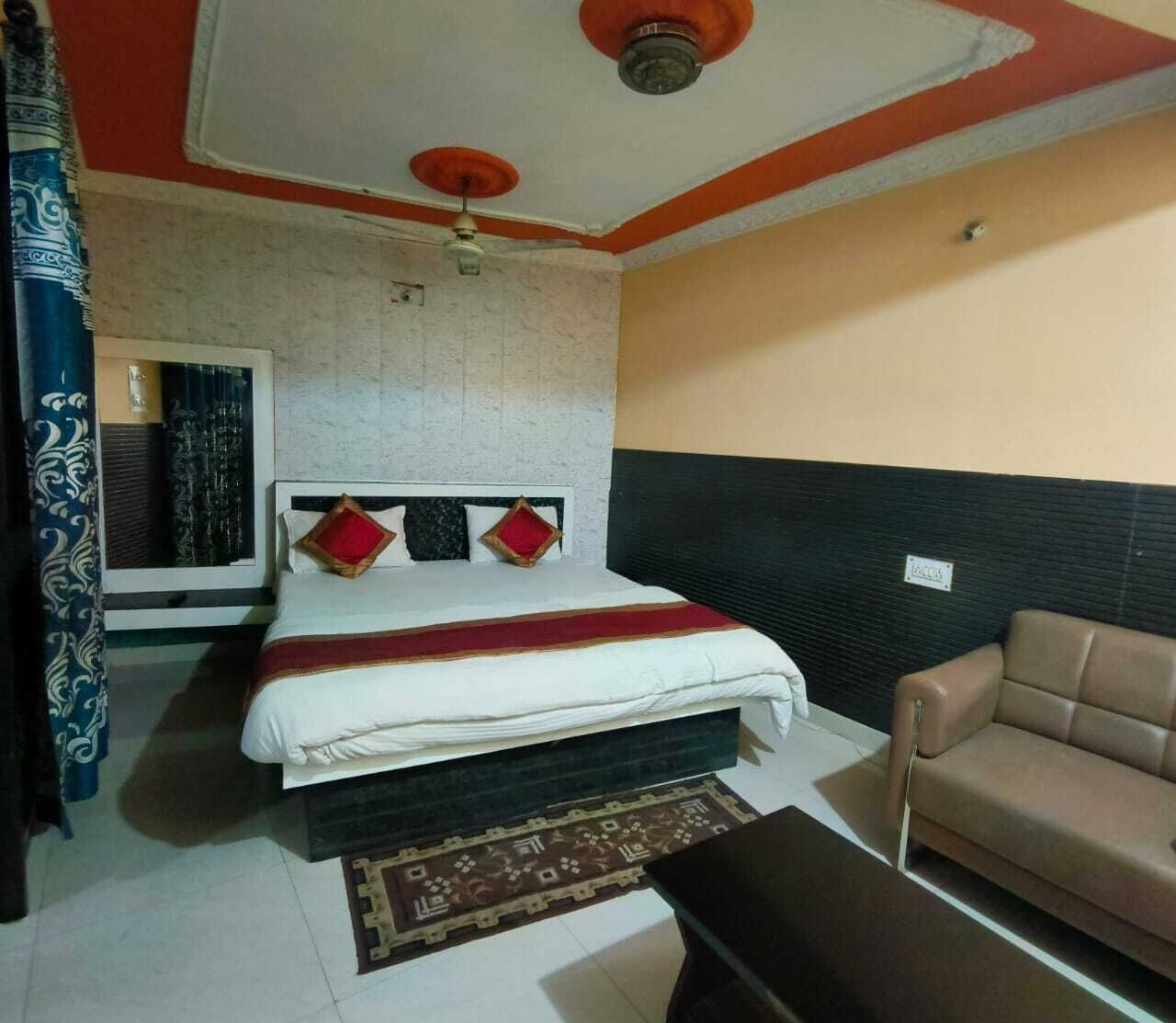 Quarto com cama, sofá, ventoinha no teto e televisão na parede.