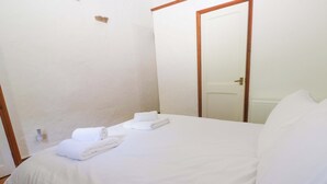 Quarto com cama bem arrumada, piso de madeira e parede branca.